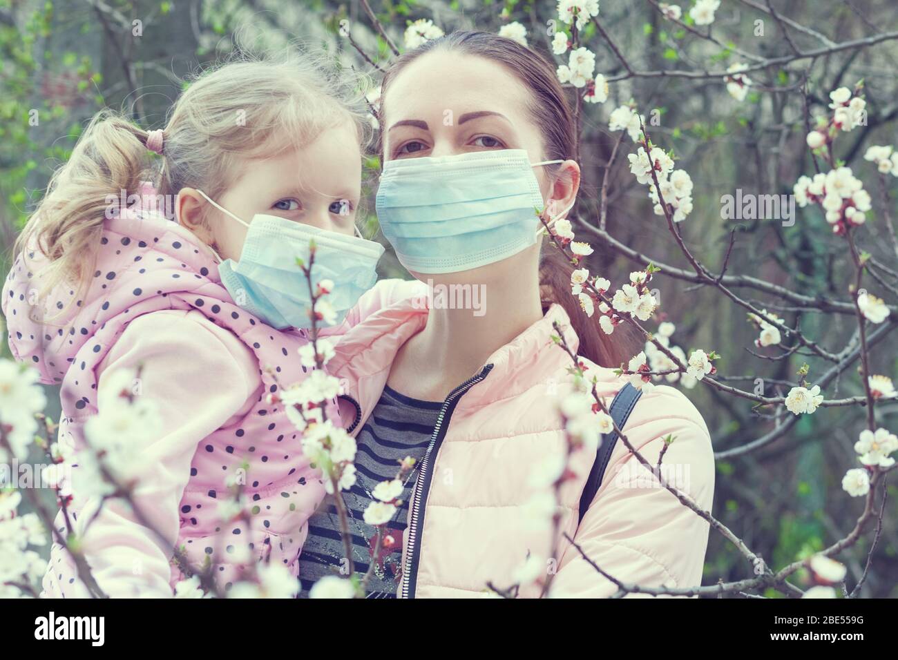 Portrait of a mom and daughter in masks on the street near a flowering ...