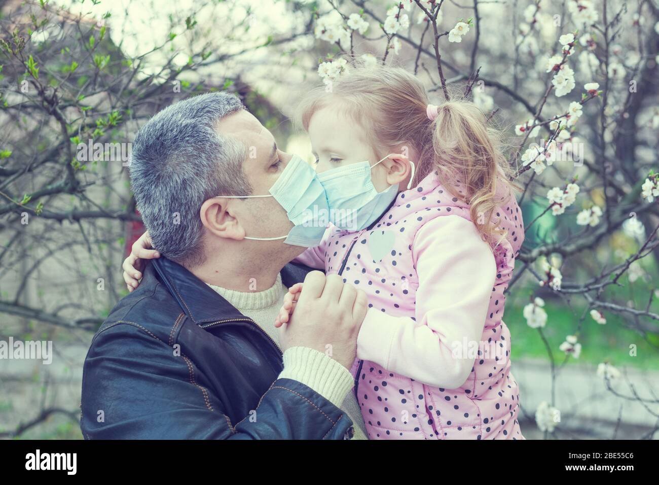 Portrait of dad and daughter in masks on the street near a flowering ...