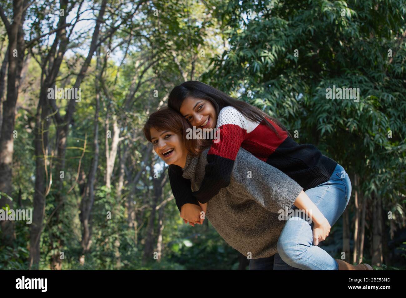 Young woman giving her younger sister a piggy back ride in the park ...