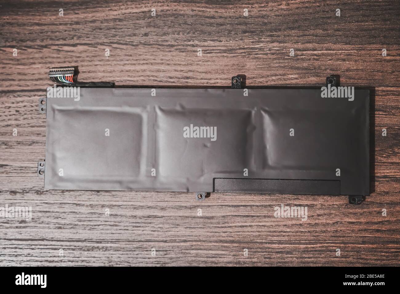 Swollen Lithium Polymer (Li-Po) laptop battery on a wooden table. Known ...