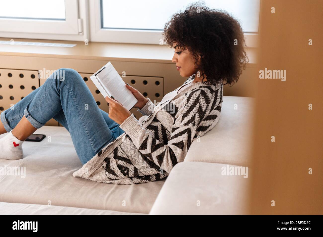 Image of a beautiful young african woman indoors at home reading book ...