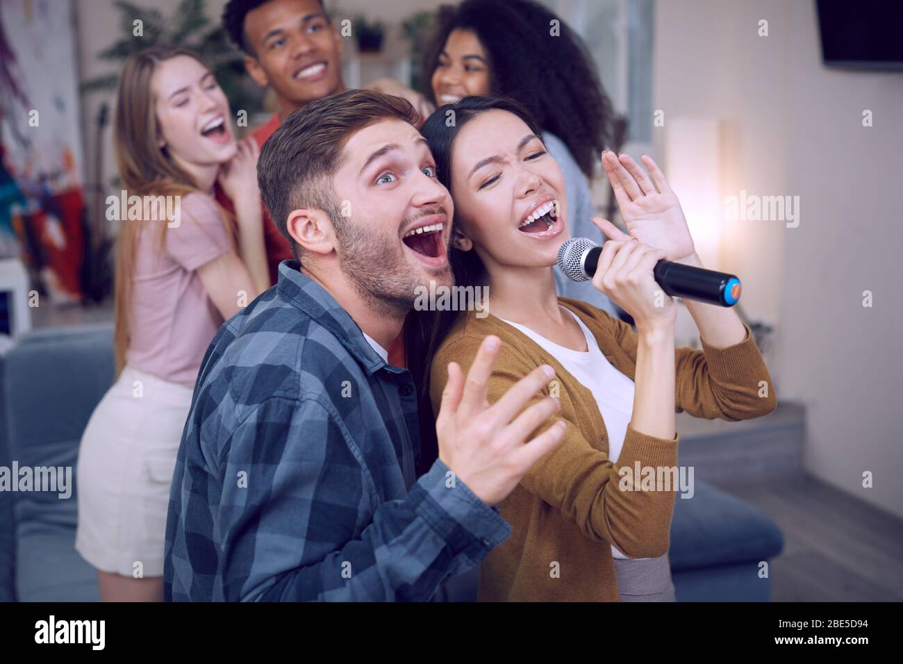 Singing duet. Young excited couple or friends holding microphone and ...