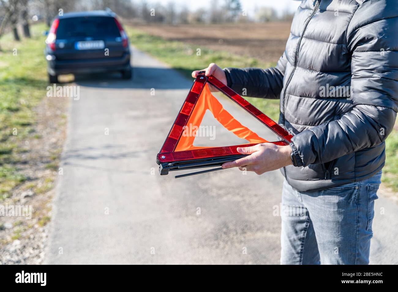 young man installs an orange warning triangle on the road in front of a ...
