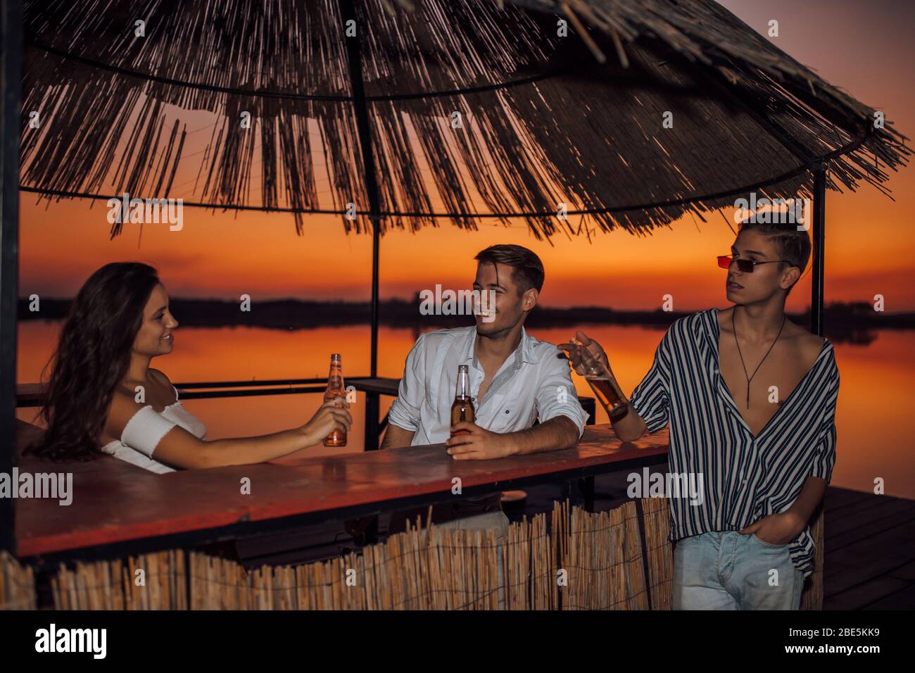 Happy friends partying on the beach bar with drinks. Happy young people ...