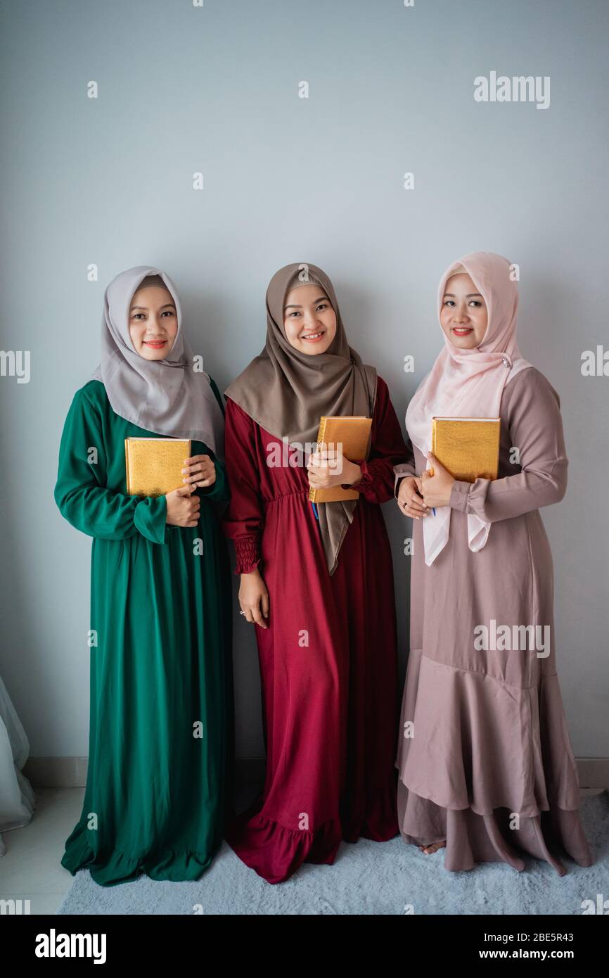 three moslem women smilling hold the holy book of Al-Quran when ...