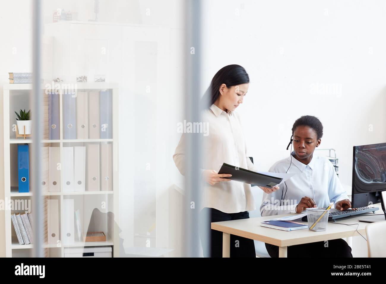 Portrait of Asian female boss talking to African-American woman while ...