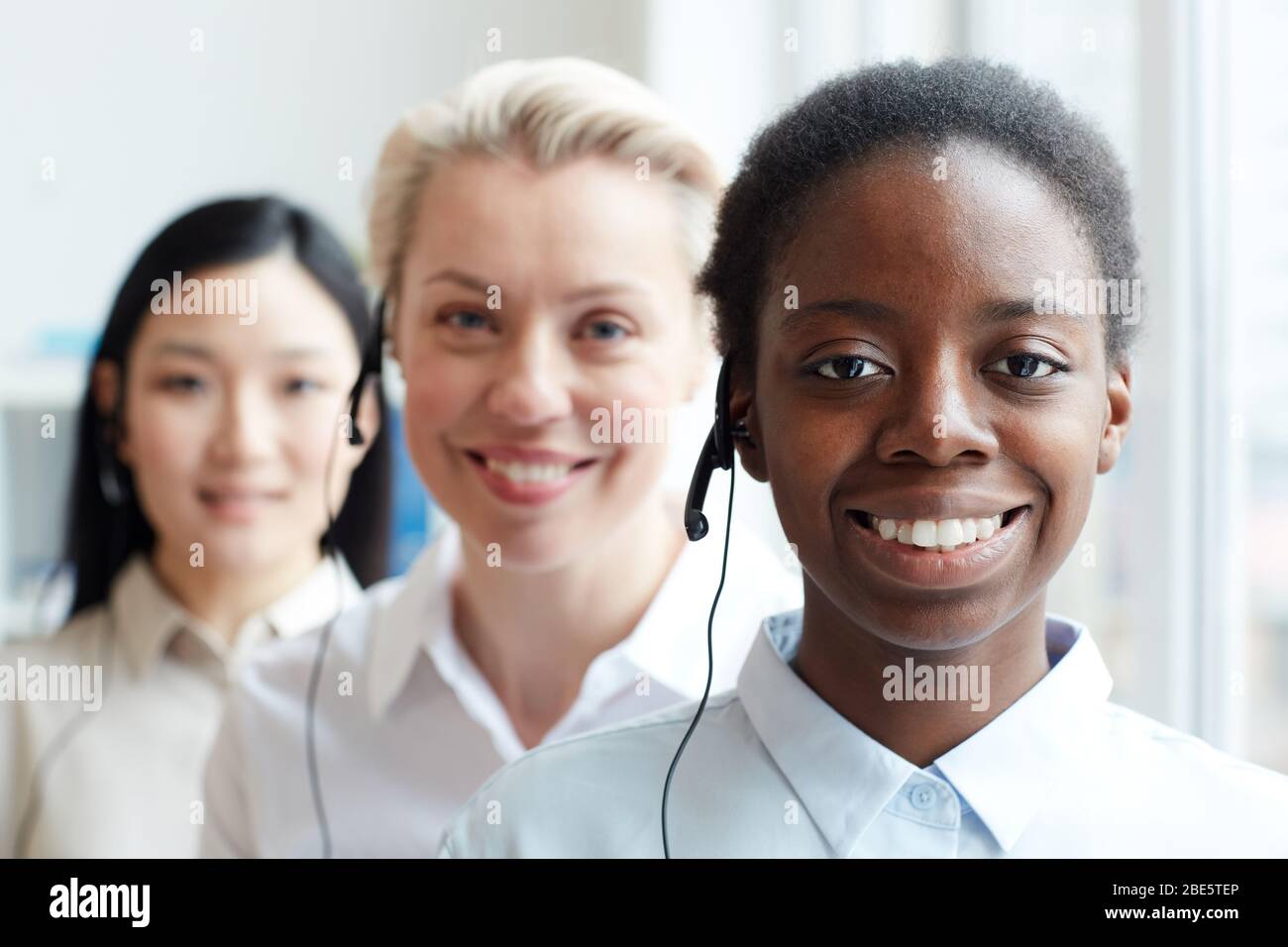 Multi-ethnic group of female call center operators looking at camera ...