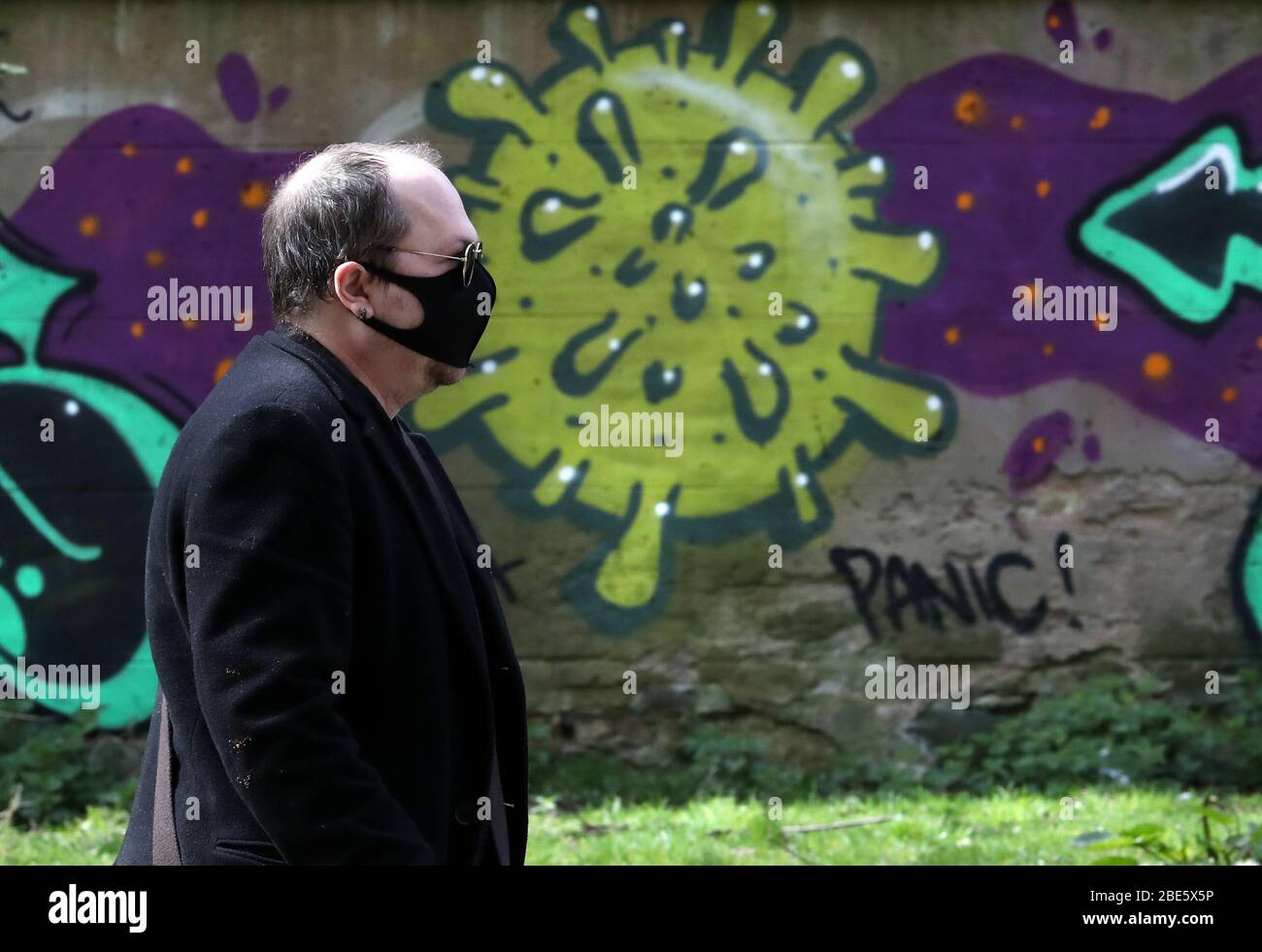 A man wearing a mask walks past coronavirus related graffiti in ...