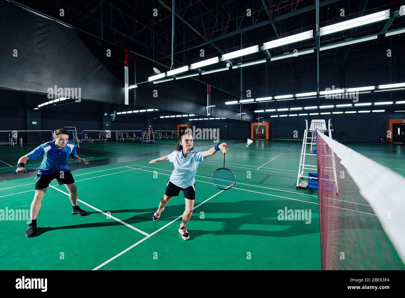 Mixed double playing badminton game, woman jumping and swinging racket ...