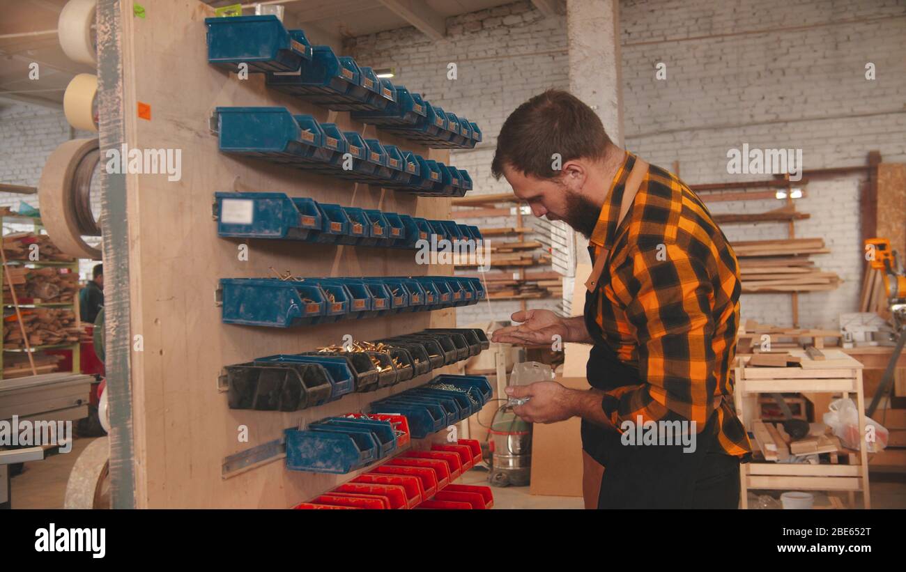 Carpentry workshop - man worker choosing screws from the stand indoors ...