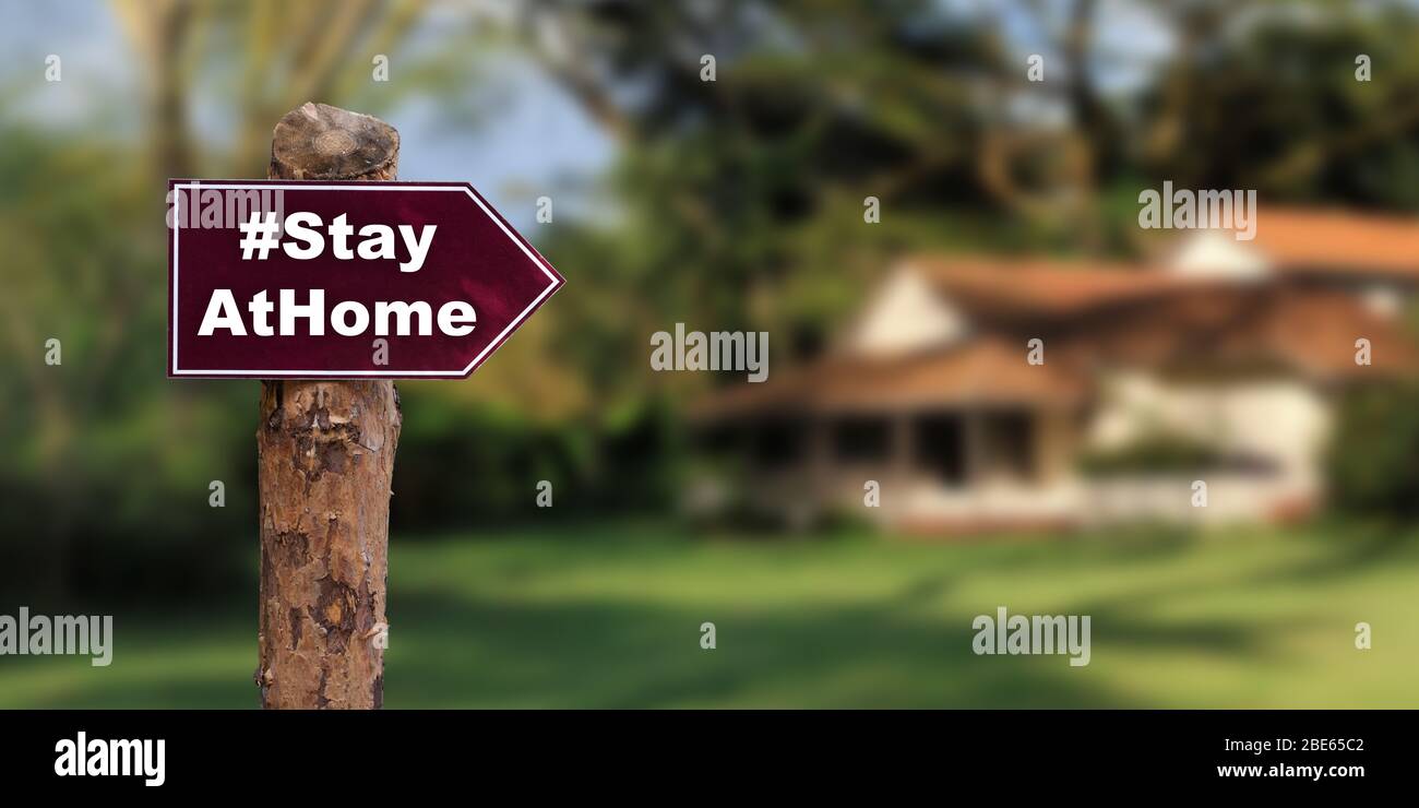 Direction board with an message Stay at home with blurred house ...