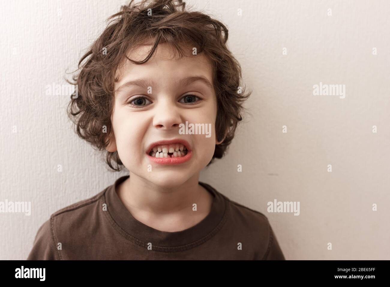 Charming curly boy smiles without tooth on white background. The boy ...