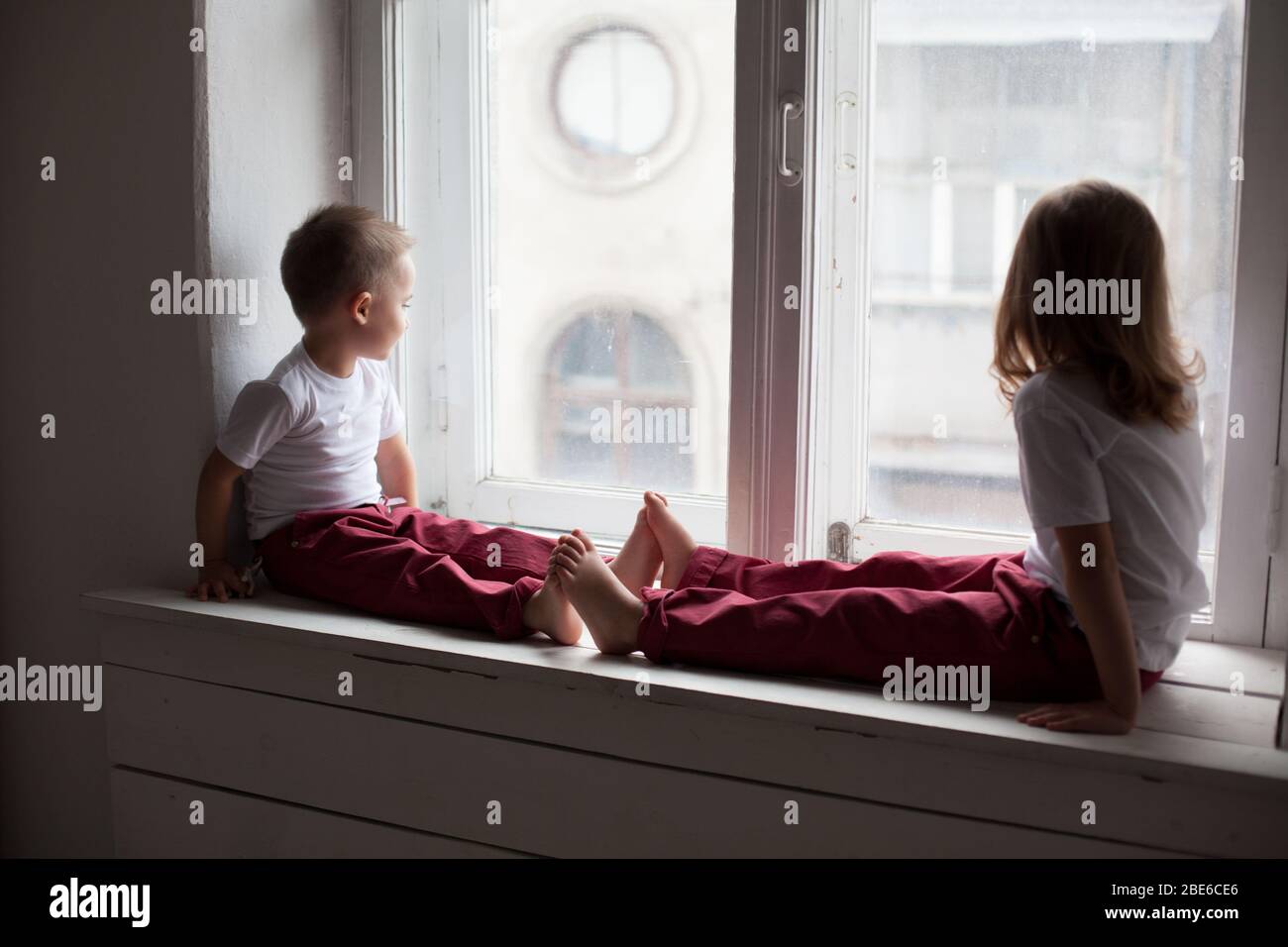 little boy and girl sitting by the window Stock Photo - Alamy