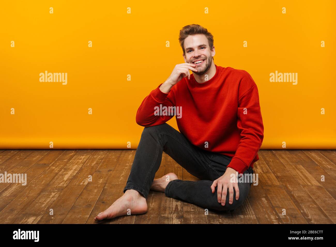 Attractive happy young man wearing pullower sitting on a floor over ...