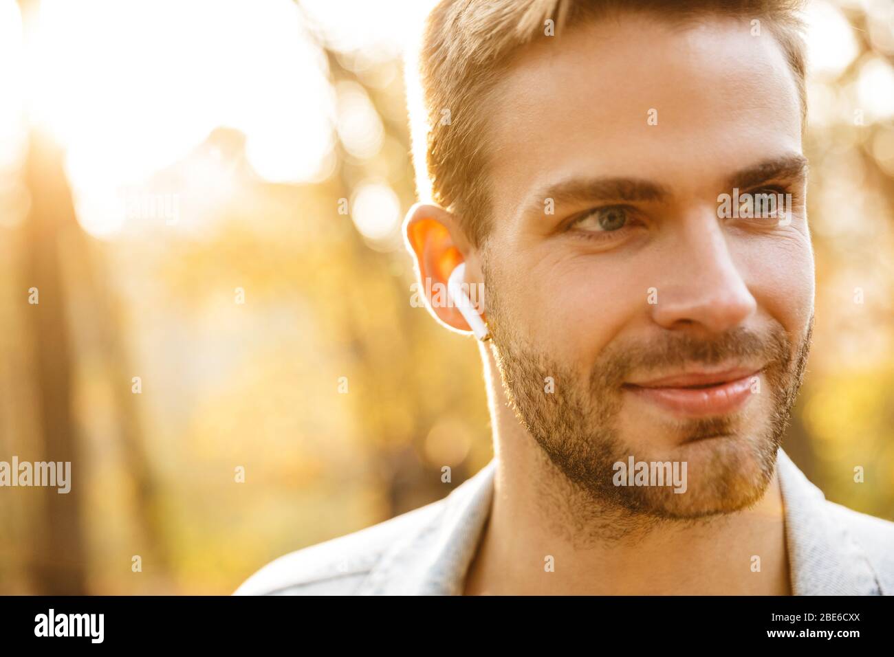 Image of handsome young caucasian man in denim jacket smiling and using ...