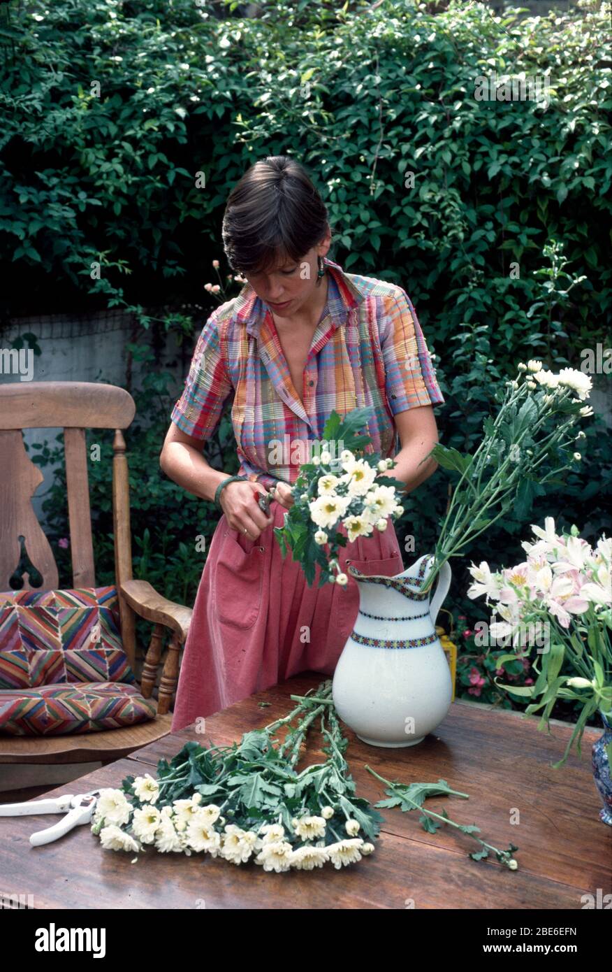 Woman arranging flowers in jug on garden tableEditorial use only Stock ...
