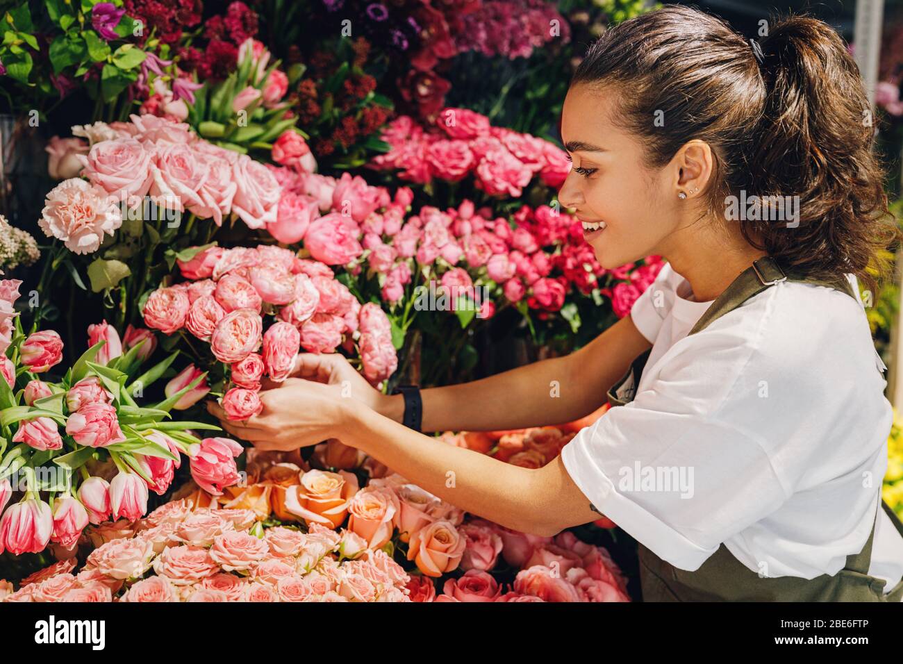 Side view of a beautiful smiling woman observing flowers in a storage ...