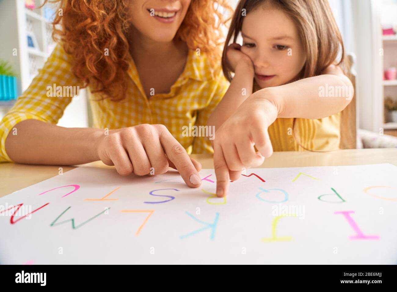 Young adult mother and her kid girl pointing on letters with fingers ...