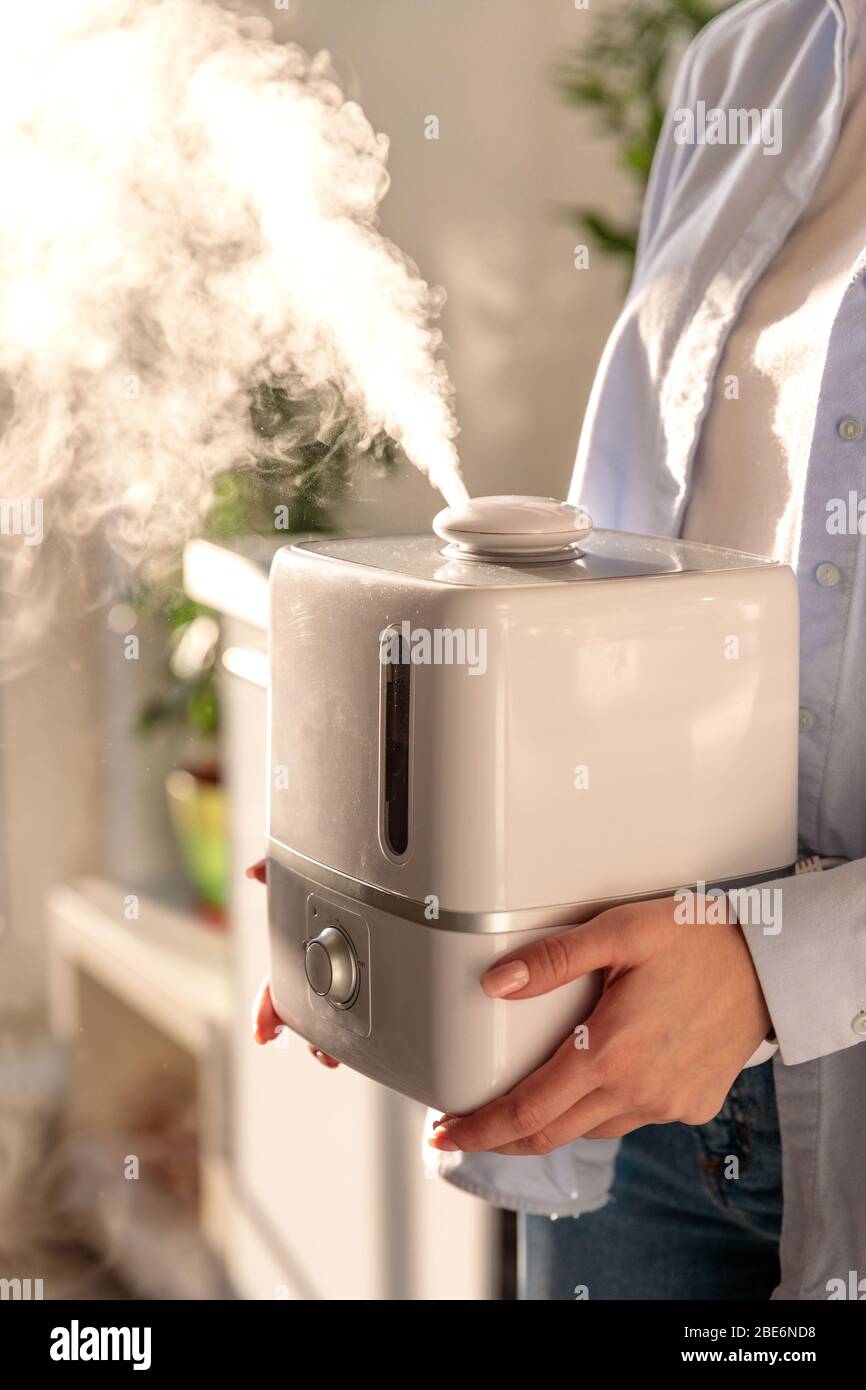 Woman holding in her hands working aroma oil humidifier in sunny room ...