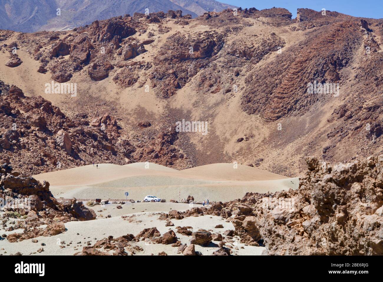 Sand in a brown crater, a street with a car, some persons not ...