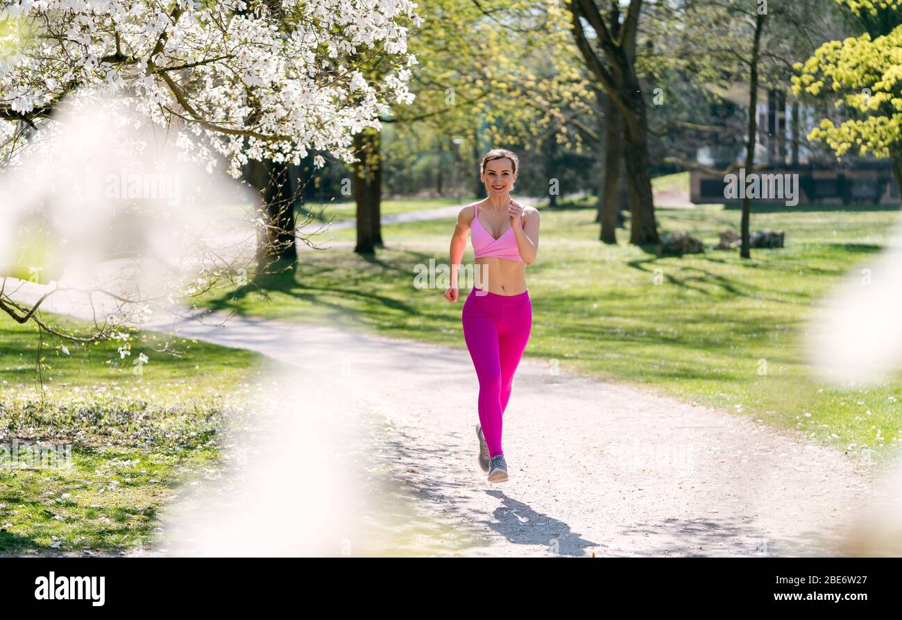 Fit woman running down a path during spring seen through blossom Stock ...