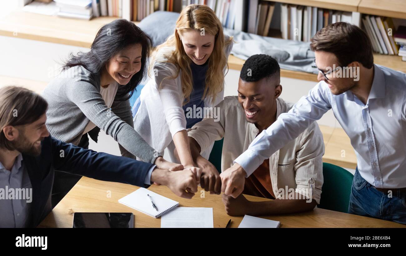 Excited multiethnic coworkers join fists engaged in teambuilding Stock ...
