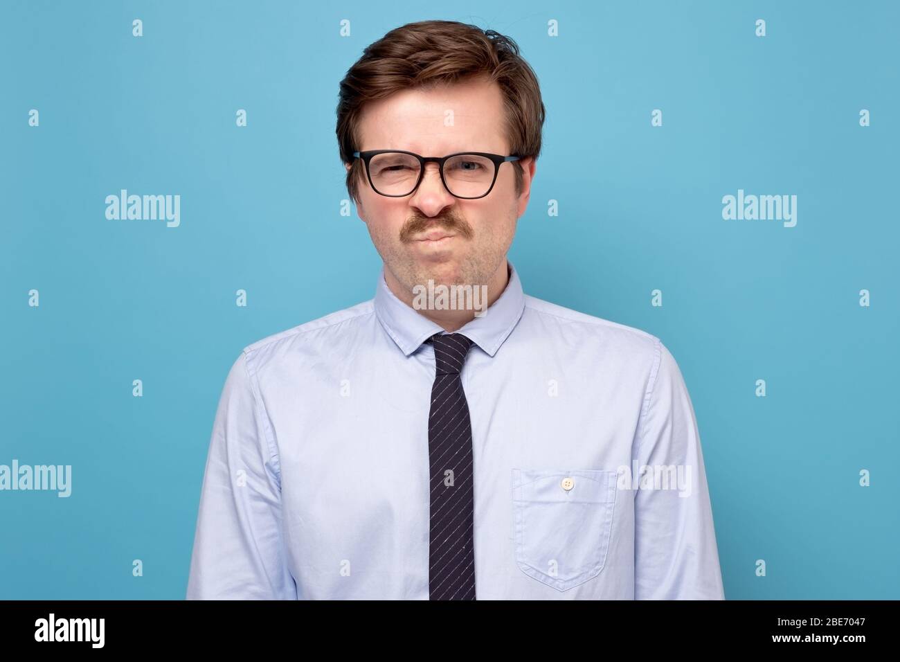 Doubtful man in spectacles, curves lips, looks directly into camera ...