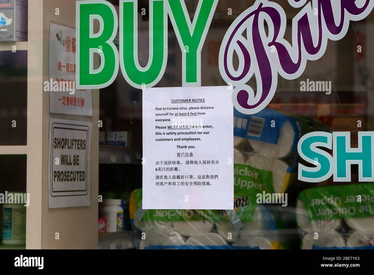 A social distancing, and wear mask safety sign taped to a window at a ...