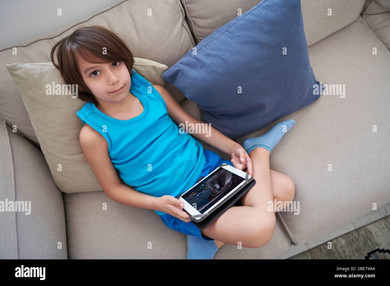 Little Arabian boy sitting on sofa and playing game on digital tablet ...
