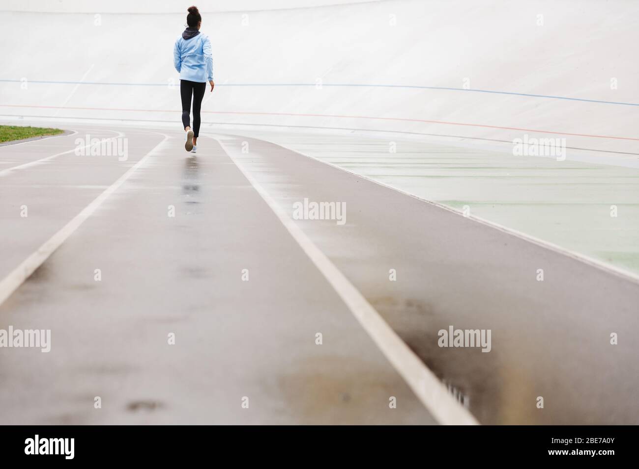 Back view of a young fit african sportswoman running at the stadium ...
