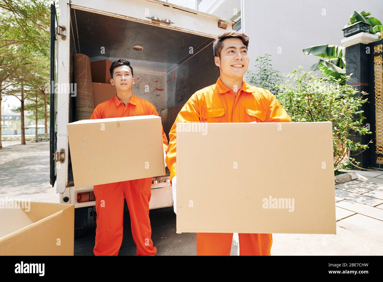 Positive Vietnamese moving service workers in orange uniform carrying ...