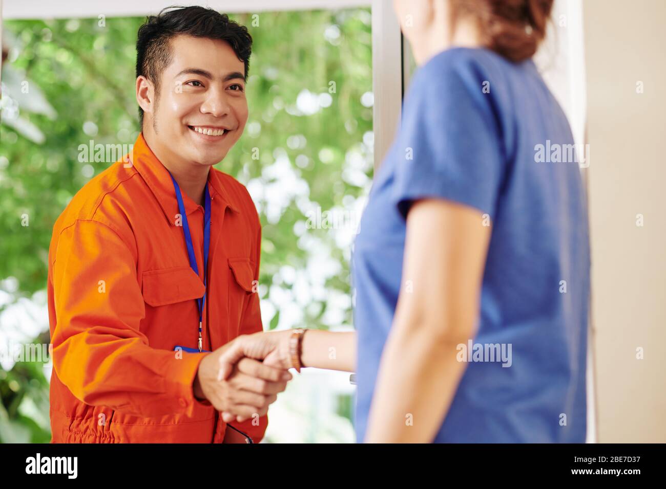 Smiling handsome Asian service worker shaking hand of female customer ...