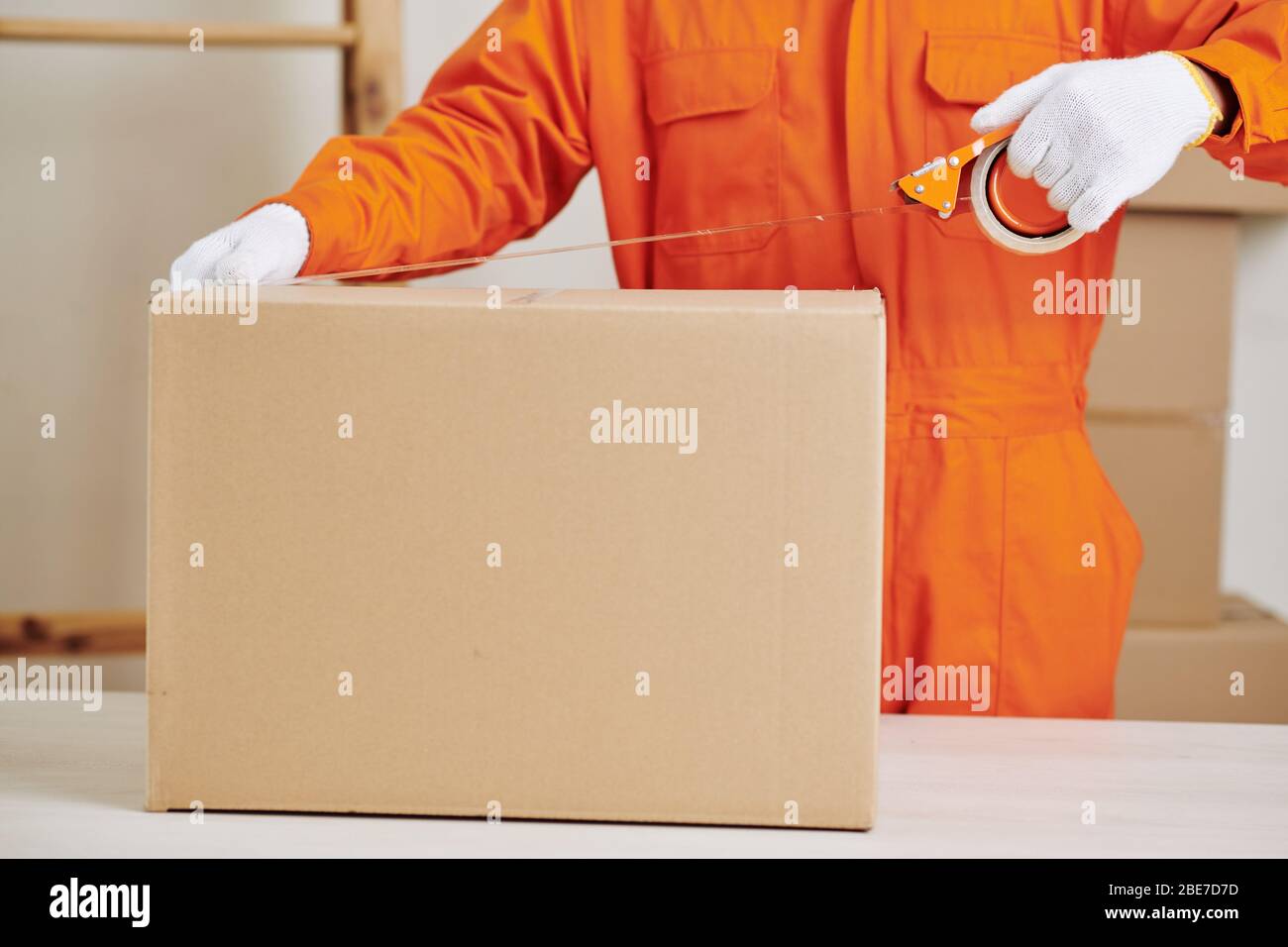 Moving service worker in uniform sealing cardboard box with adhesive ...