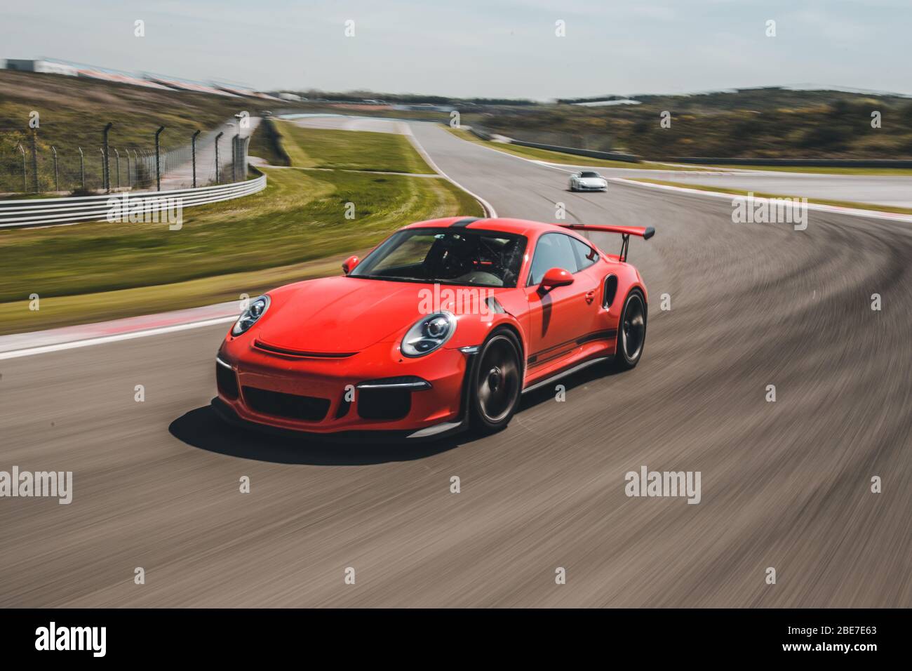 Red sport car racing on the trace with other cars across green fields ...