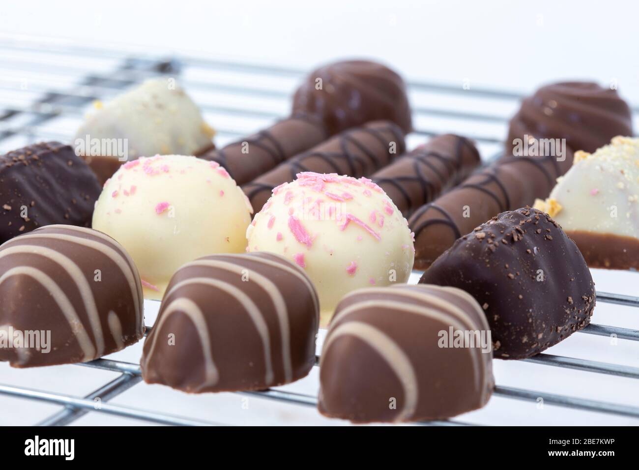 Selection of chocolates on a metal cooling rack. On a white wood ...