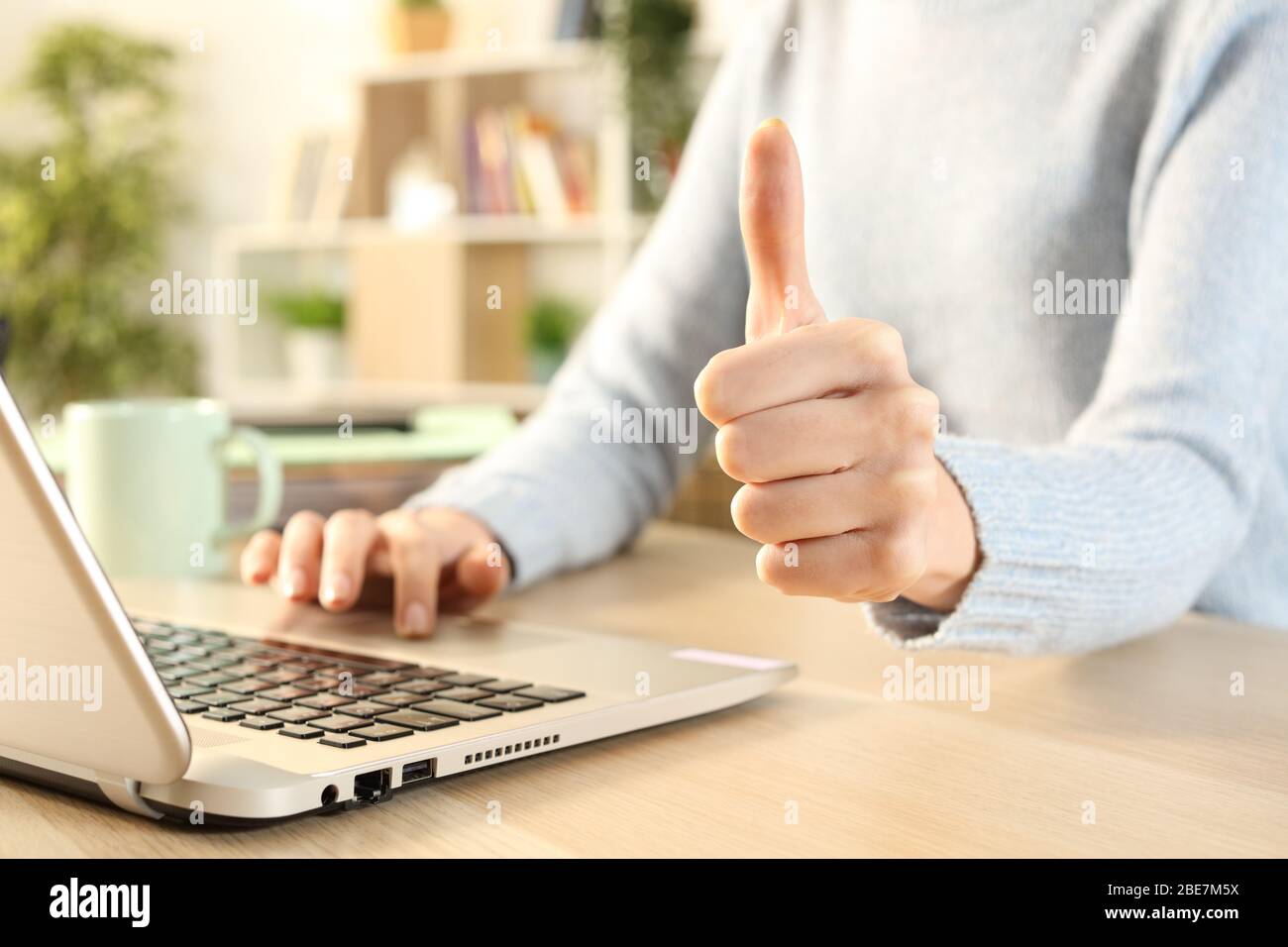 Close up of girl hands gesturing thumbs up using laptop on a desk at ...