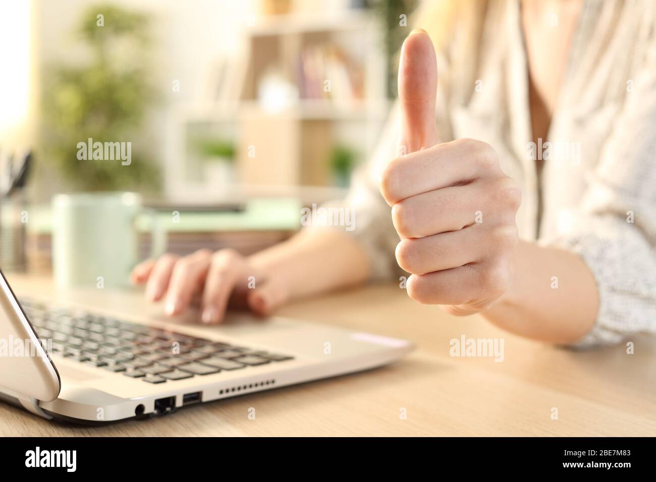 Close up of woman hands using laptop with thumbs up sitting on a desk ...