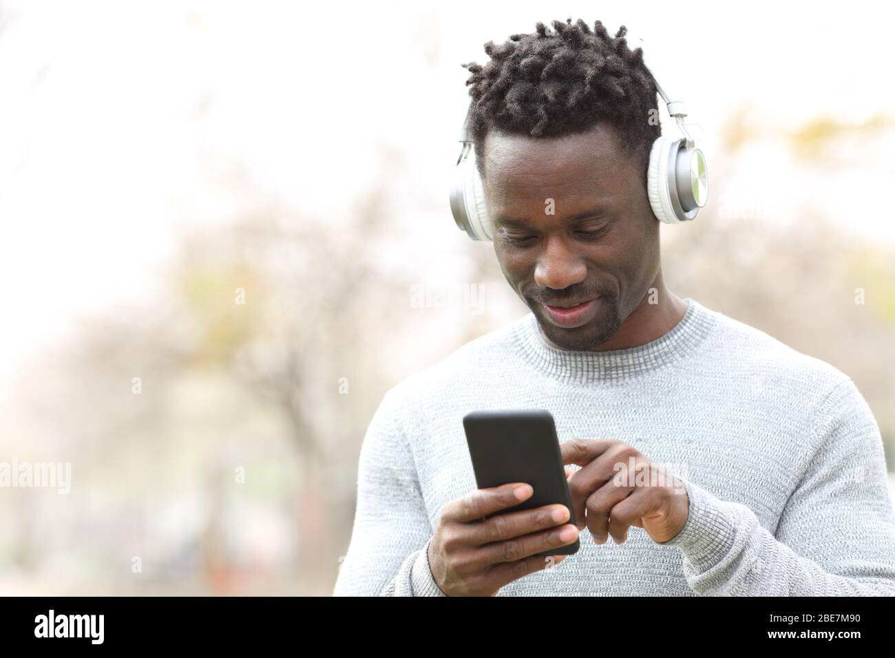 Happy black man listening music on smart phone with headphones in the ...