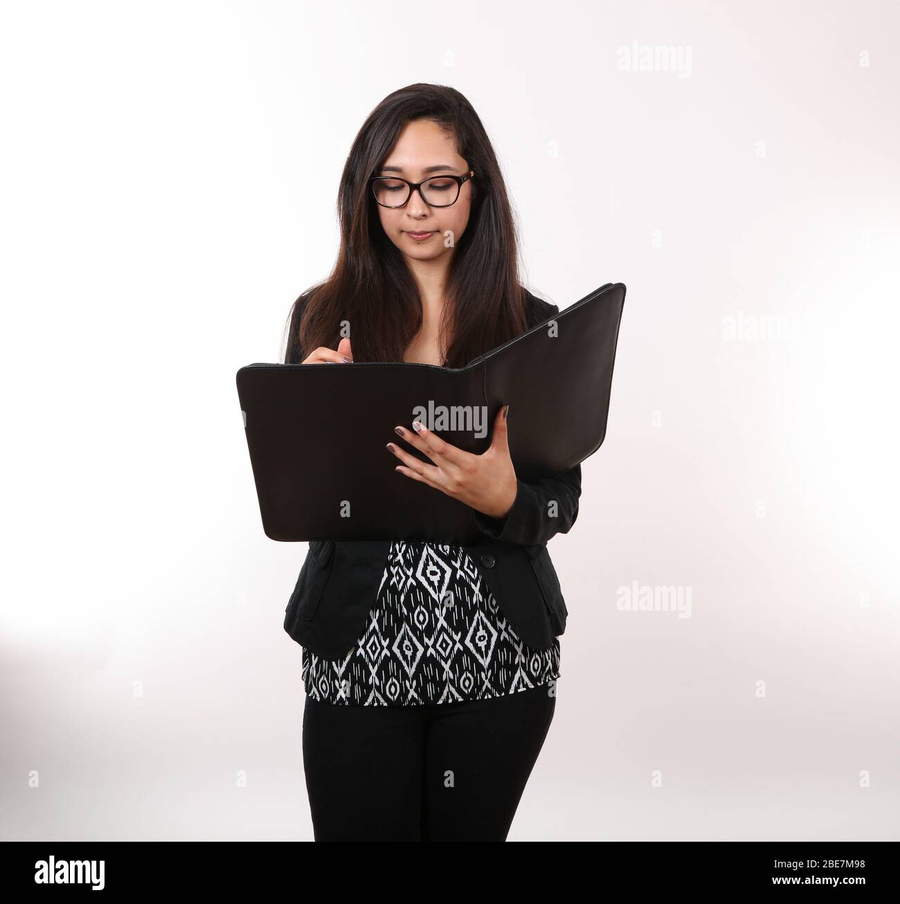 A young professional woman wearing glasses takes notes in her portfolio ...