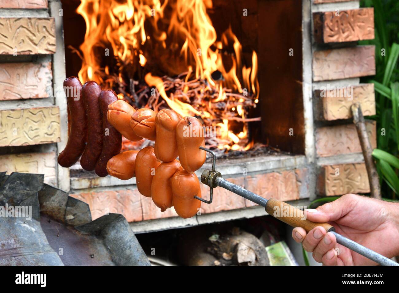 Man roasts meat sausages in a brick fireplace at the cottage Stock ...