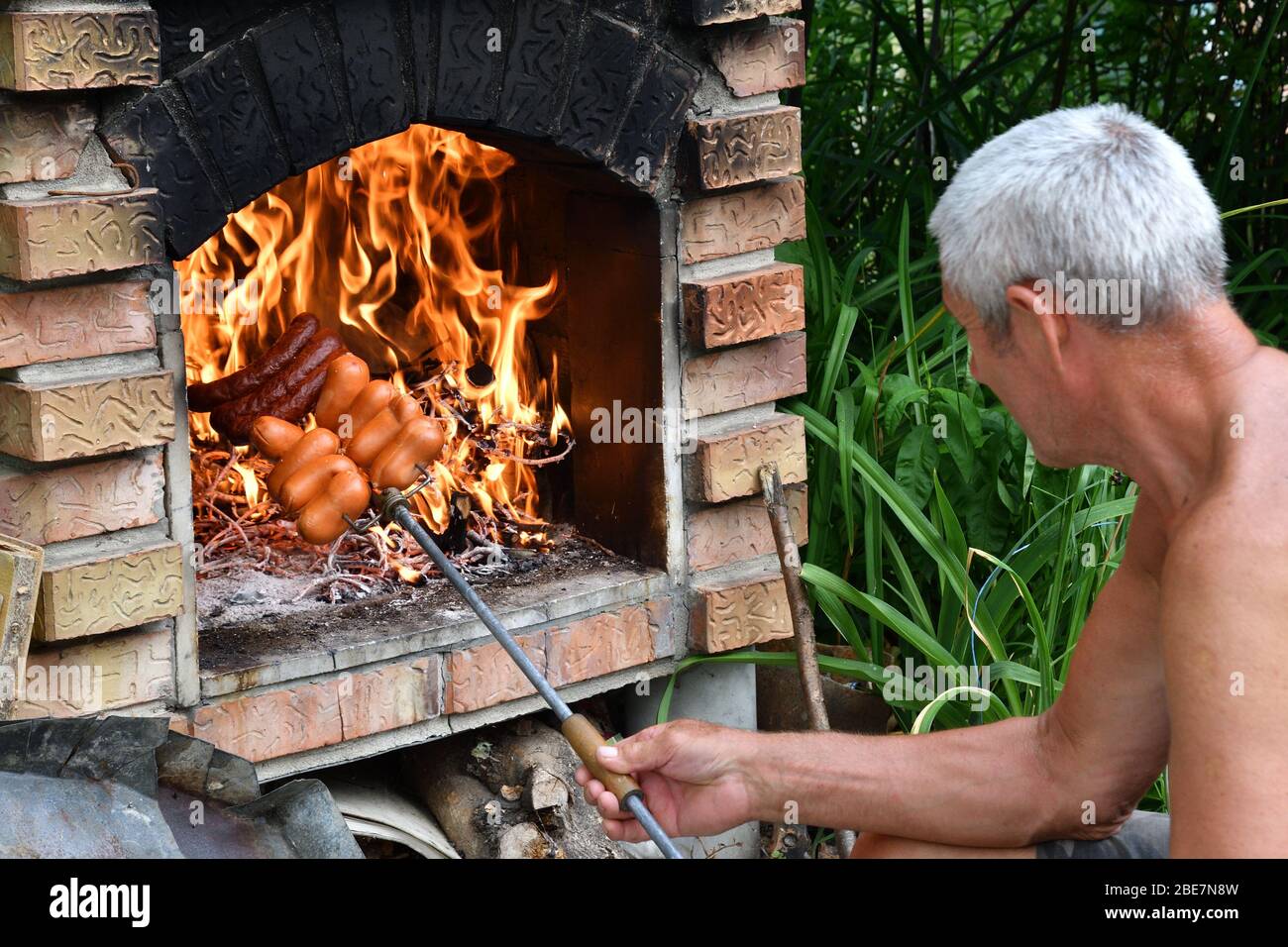 Man roasts meat sausages in a brick fireplace at the cottage Stock ...