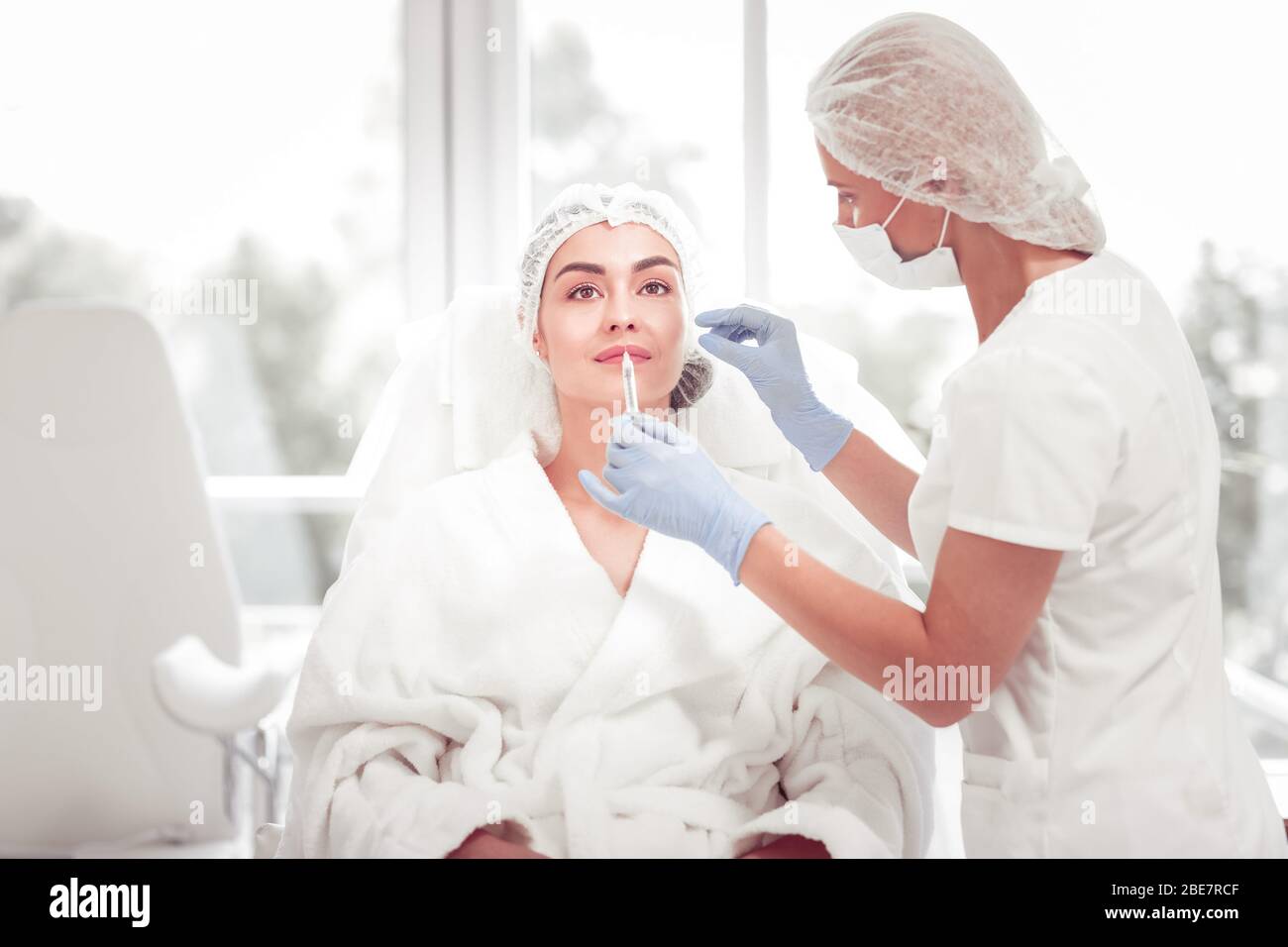 Shot into lip. Cosmetologist wearing blue gloves and white uniform ...