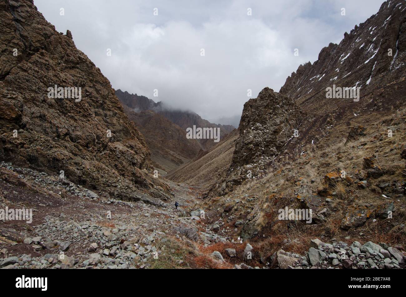 Hiker climbs down a rocky footpath in a canyon between two mountain ...