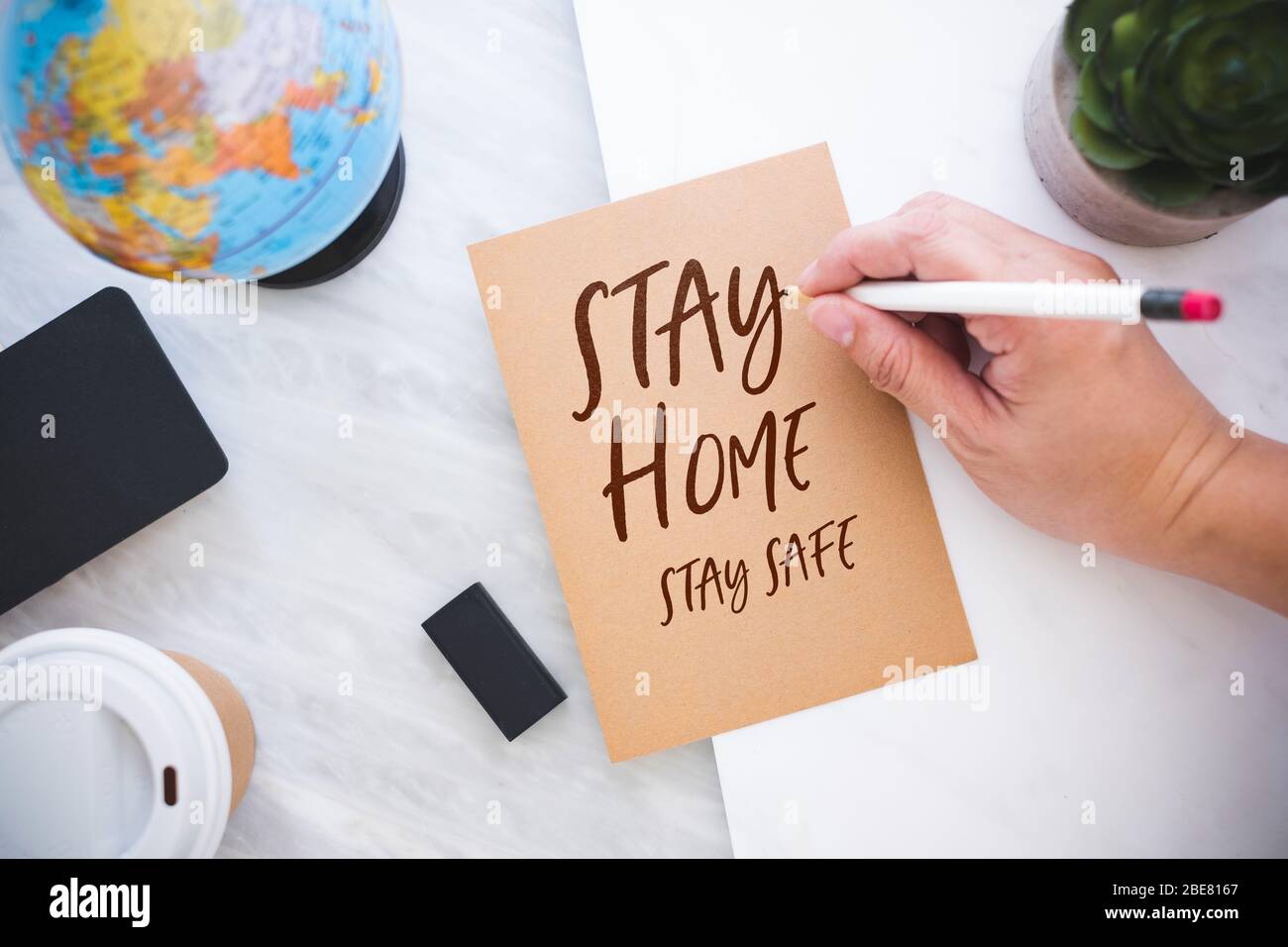Hand holding pen writing stay home stay safe on brown paper with blue ...