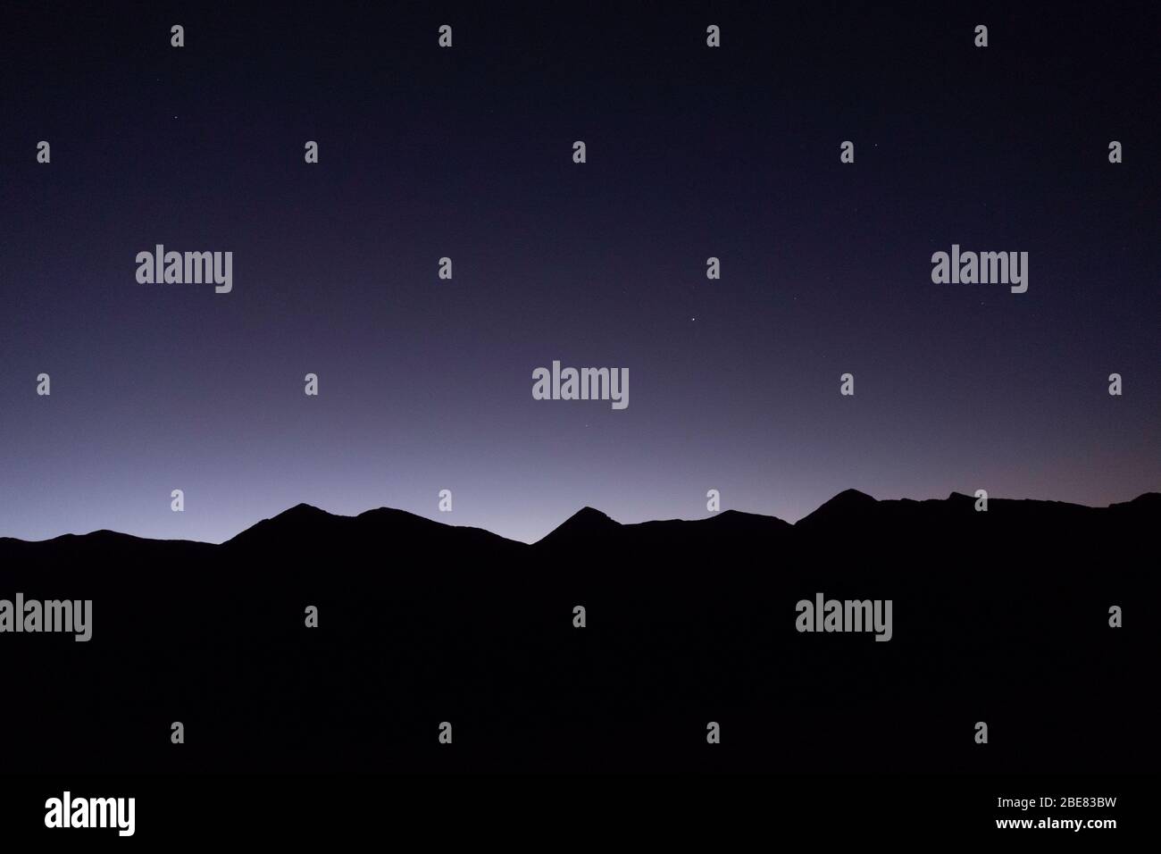 A black mountain ridge-line as silhouette against the dark blueish ...