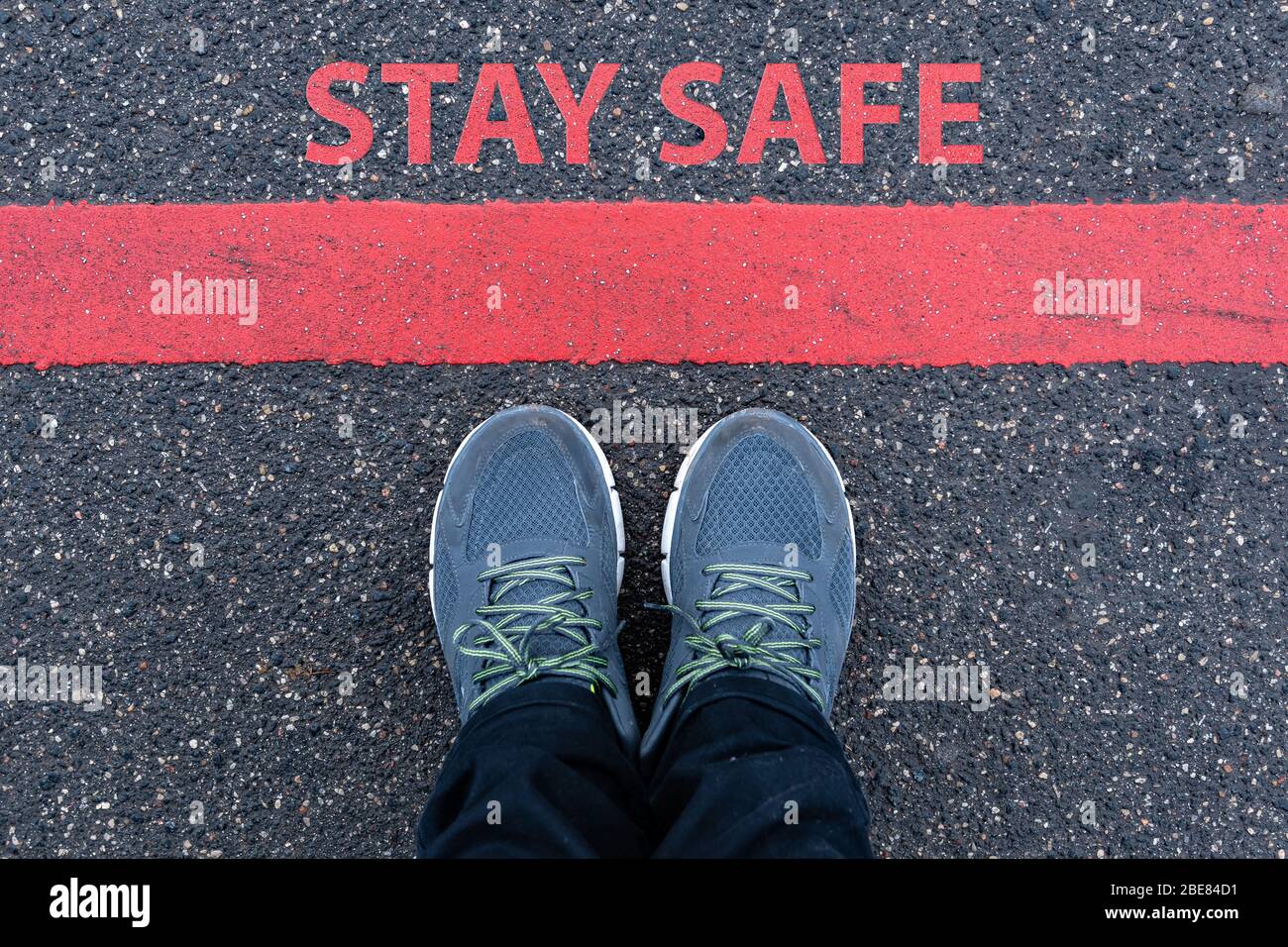 man in sneakers standing next to a red line with text STAY SAFE ...