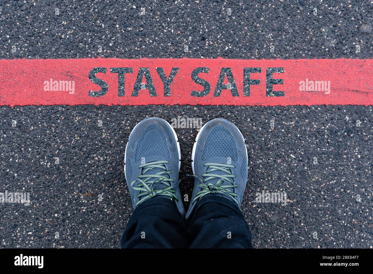man in sneakers standing next to a red line with text STAY SAFE ...