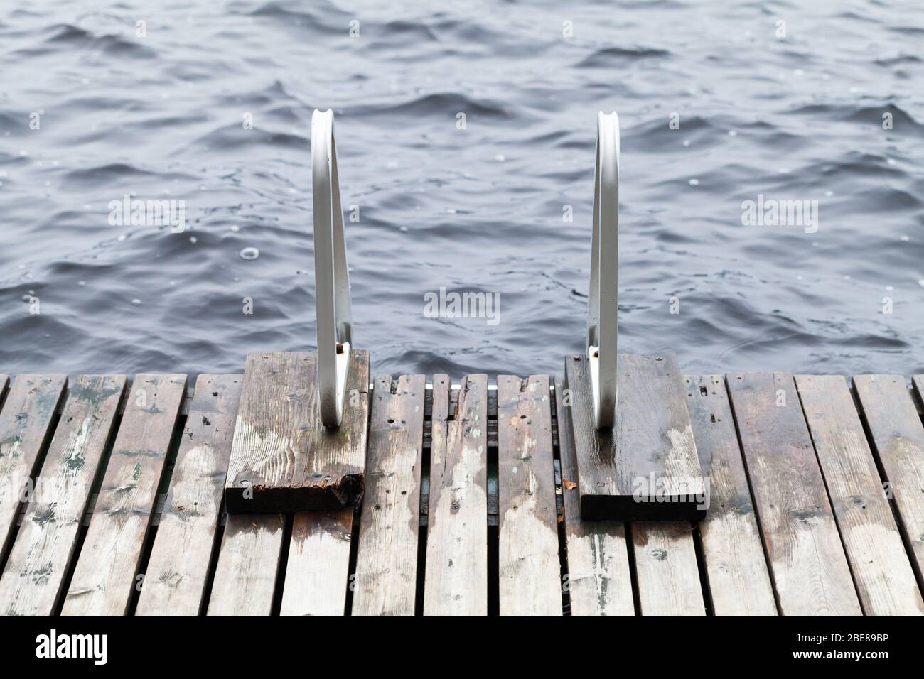 Wooden pier edge with metal rails for swimming on a still lake coast ...