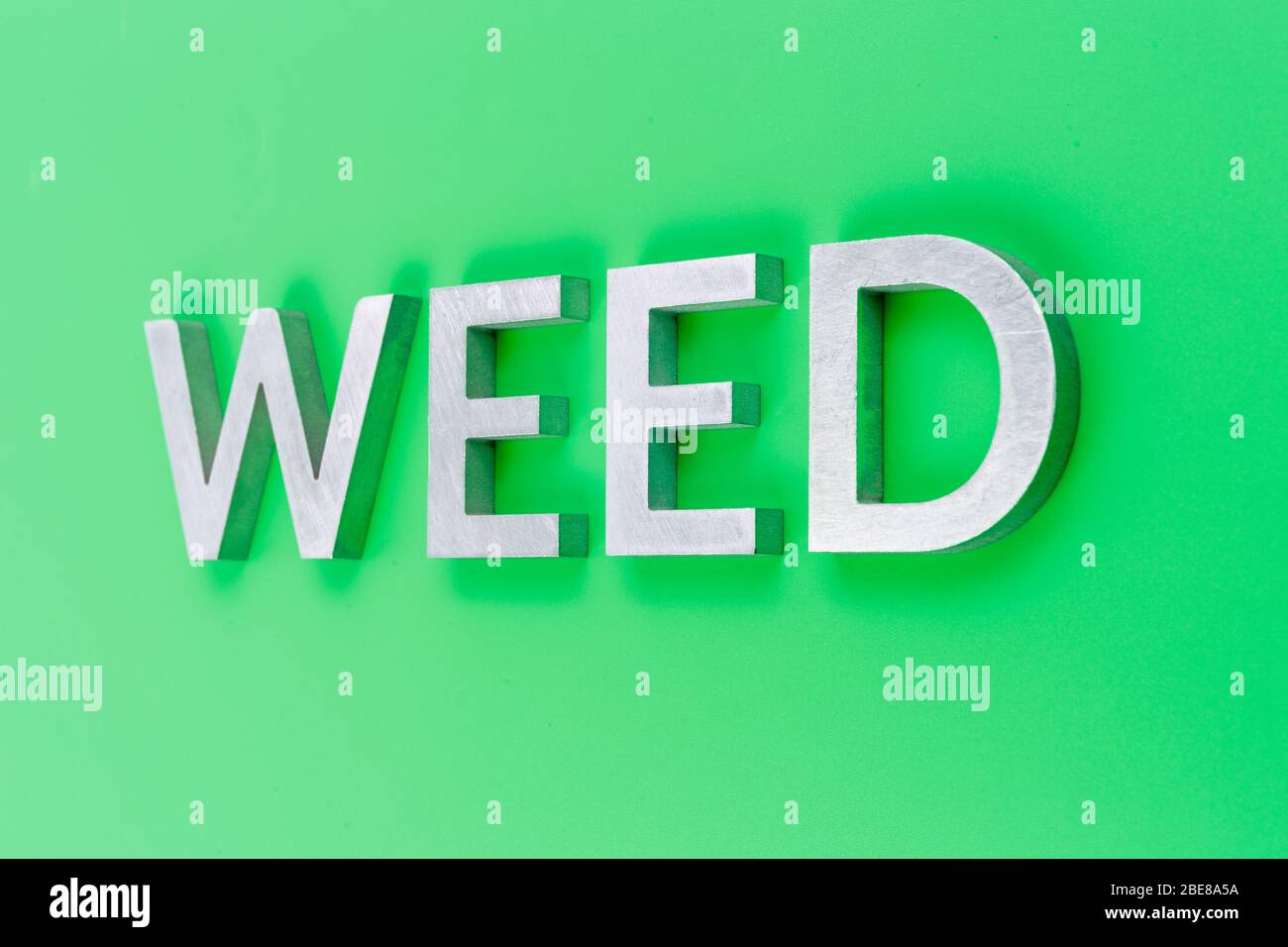 the word weed laid with silver metal letters on pastel green background ...