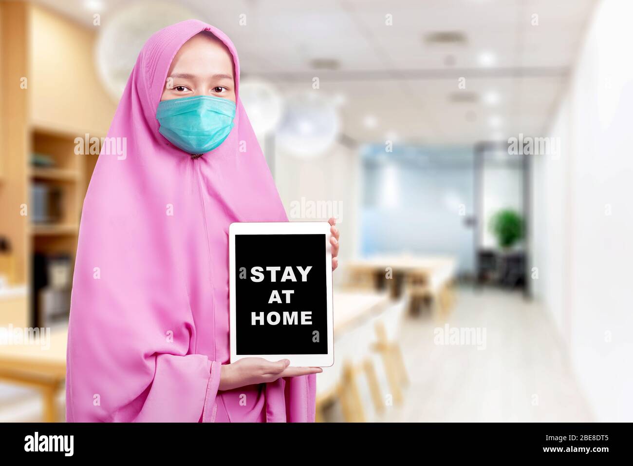 Asian Muslim woman in a veil and wearing a flu mask showing tablet with ...